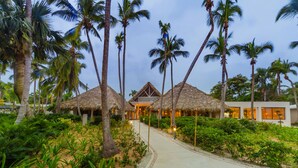Um resort com cabanas de telhado de palha, palmeiras e um caminho pavimentado.