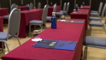Uma sala de conferências com mesas cobertas por toalhas vermelhas, cadeiras e uma garrafa azul sobre uma das mesas.