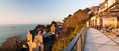 Um deck de madeira com vista para uma vila costeira, edifícios de pedra e o mar.