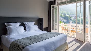 Quarto de hotel com uma cama grande, vista para uma paisagem montanhosa e uma varanda com área de estar externa.