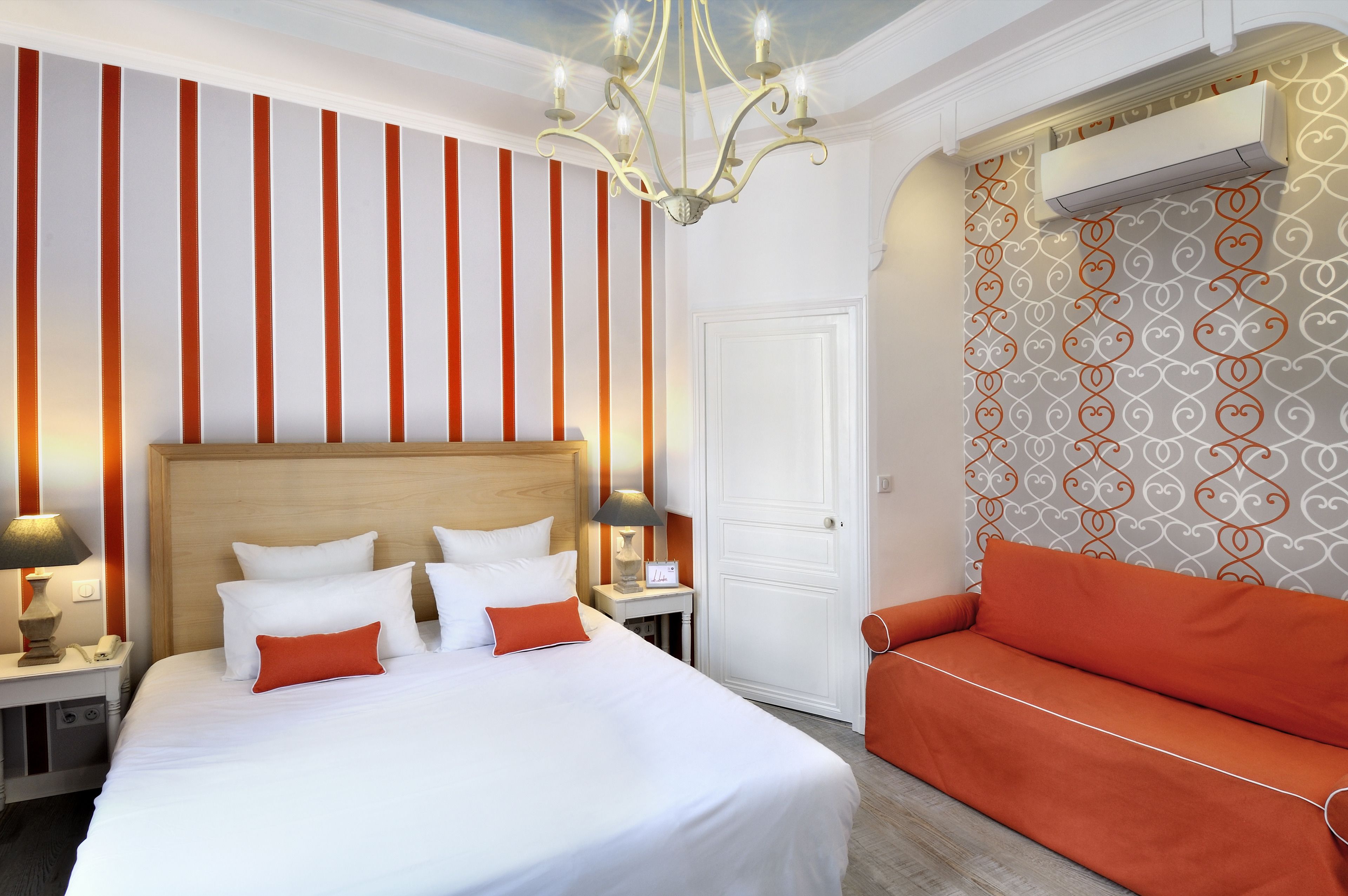 Quarto de hotel com uma cama grande, um sofá, um candelabro e paredes listradas.