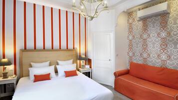 Quarto de hotel com uma cama grande, um sofá, um candelabro e paredes listradas.