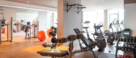 Uma academia com diversos equipamentos de exercício, incluindo esteiras, bicicletas ergométricas e pesos livres.