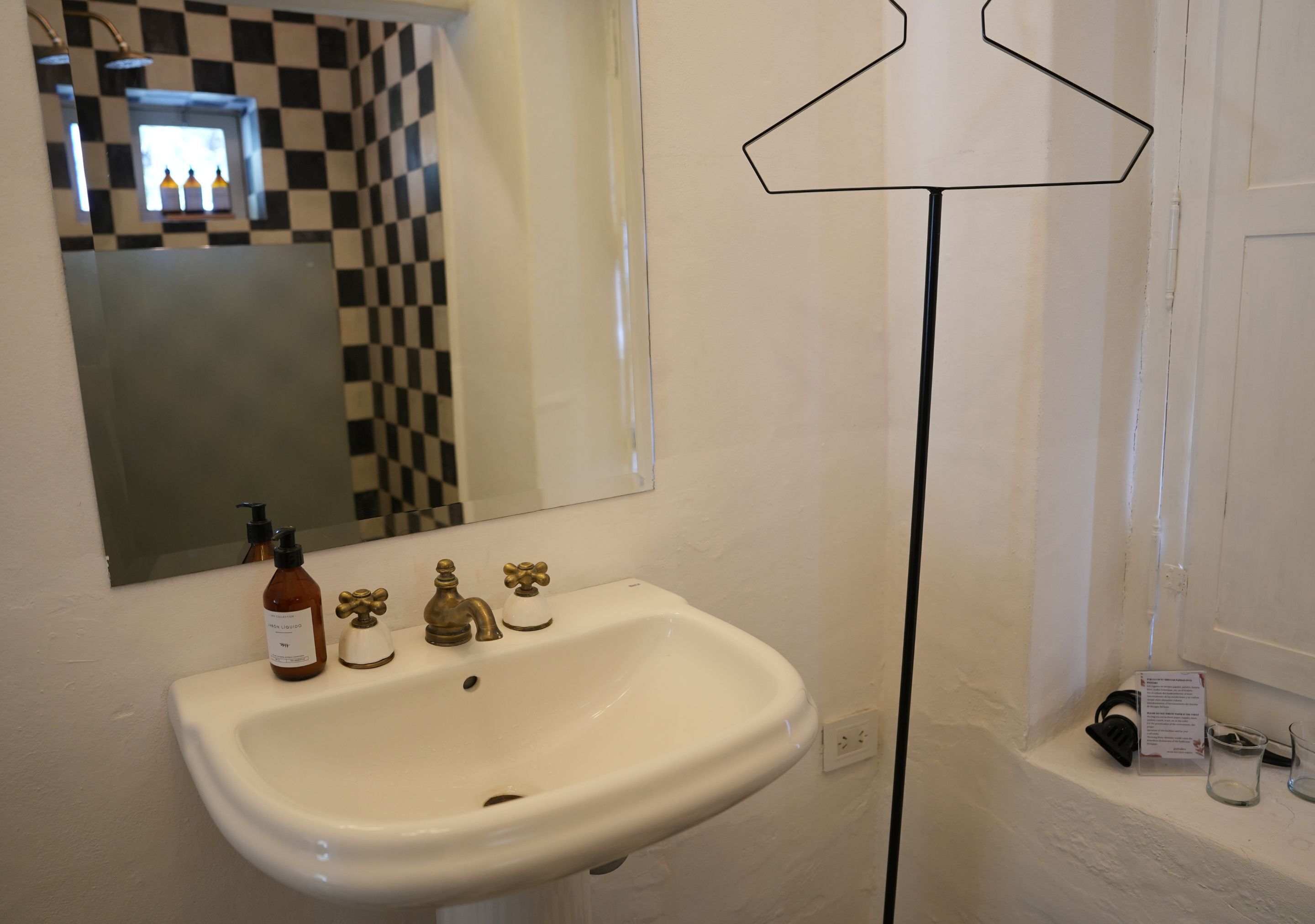 Casa de banho com uma pia branca, espelho, parede xadrez e zona de duche.