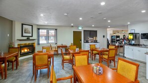 Uma sala de jantar de hotel com mesas e cadeiras de madeira, uma lareira e uma área de cozinha com eletrodomésticos.
