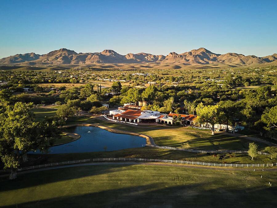 Um campo de golfe com um clube, um lago e montanhas ao fundo.