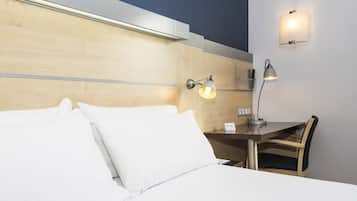 Quarto de hotel com uma cama, uma escrivaninha e duas luminárias fixadas na parede.