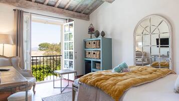 Quarto com cama, escrivaninha e cadeira, varanda com vista e estante azul com cestos.
