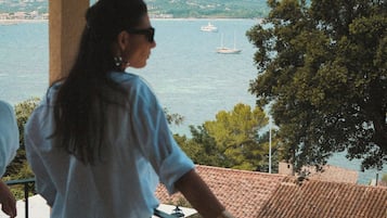 Uma varanda com vista para o mar, um barco e colinas ao longe.