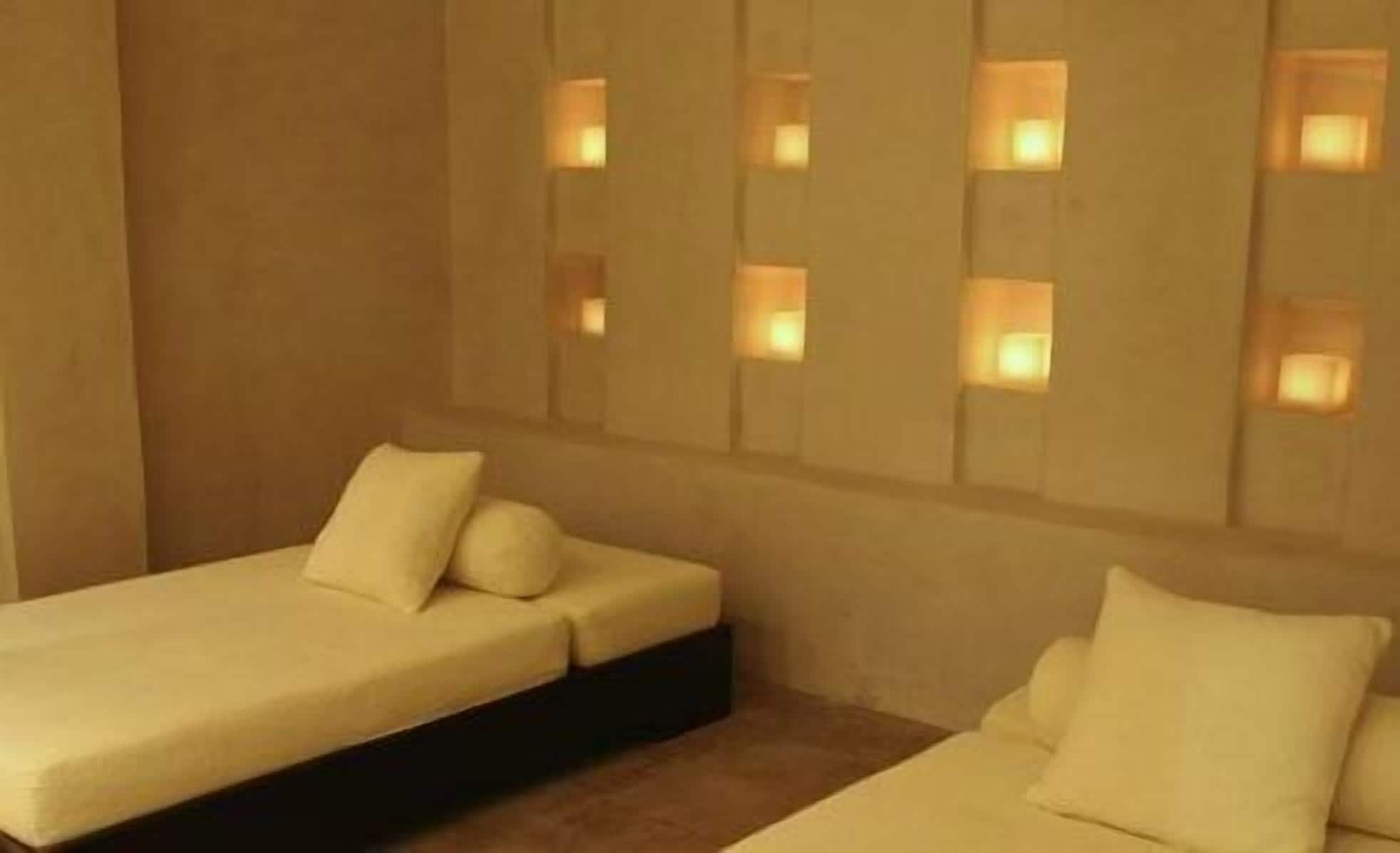 Quarto com duas camas, cada uma com travesseiro e cabeceira. H á luminárias fixadas na parede acima das camas.