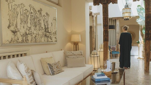 Sala de estar com um sofá branco, uma mesa de centro com livros, uma luminária e uma grande obra de arte emoldurada na parede.