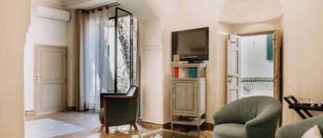 Uma sala de estar com uma mesa de centro de vidro, duas poltronas, uma televisão e um armário.