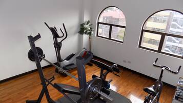 Uma academia com aparelhos de cardio, equipamentos de musculação e um banco.