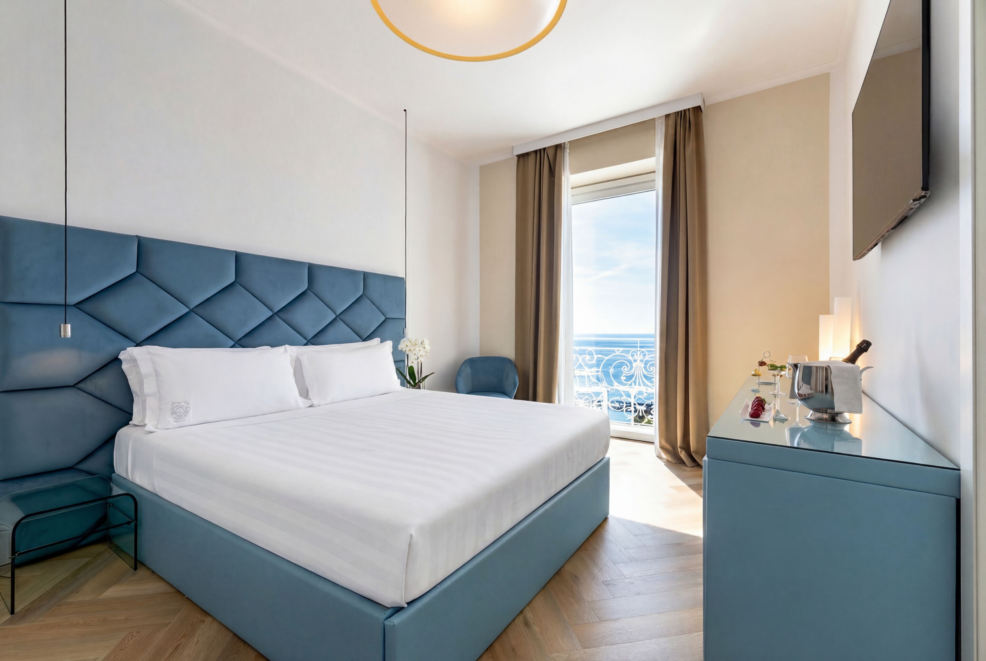 Quarto de hotel com cama, escrivaninha, cadeira e vista para a varanda.