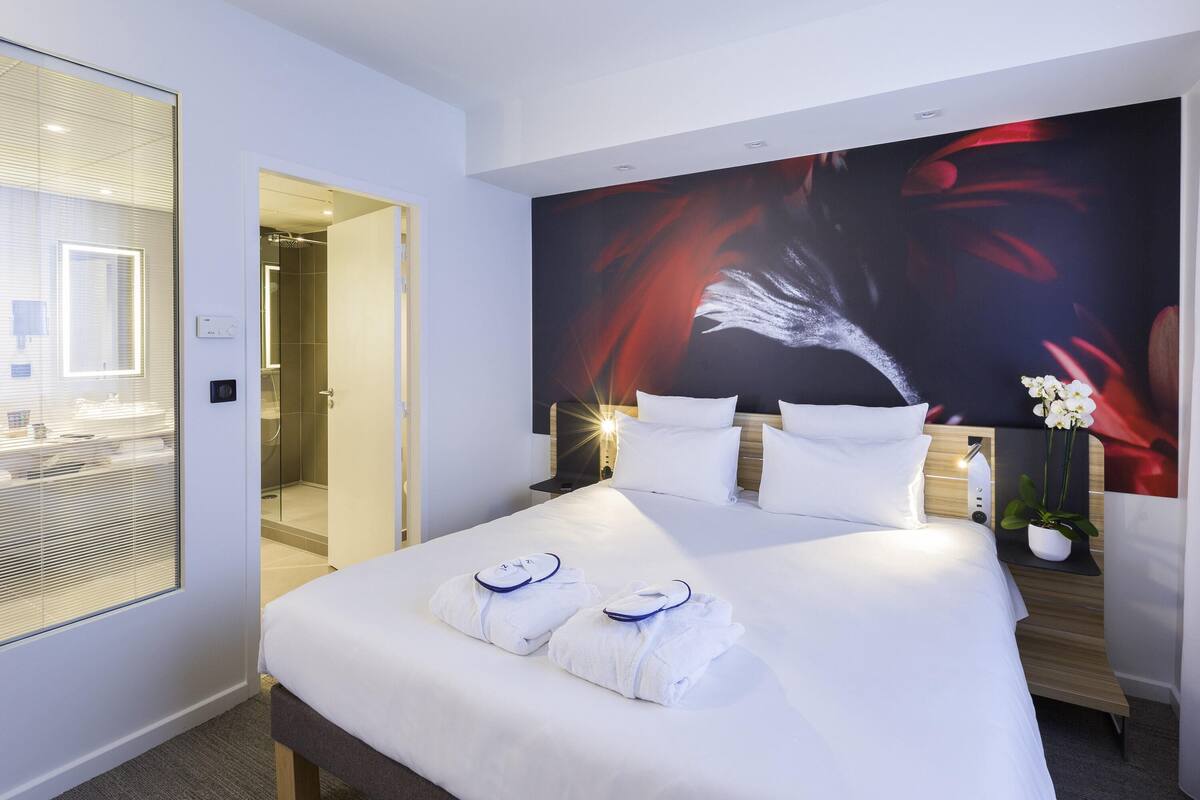Quarto de hotel com uma cama grande, televisão fixada na parede e porta para um banheiro.