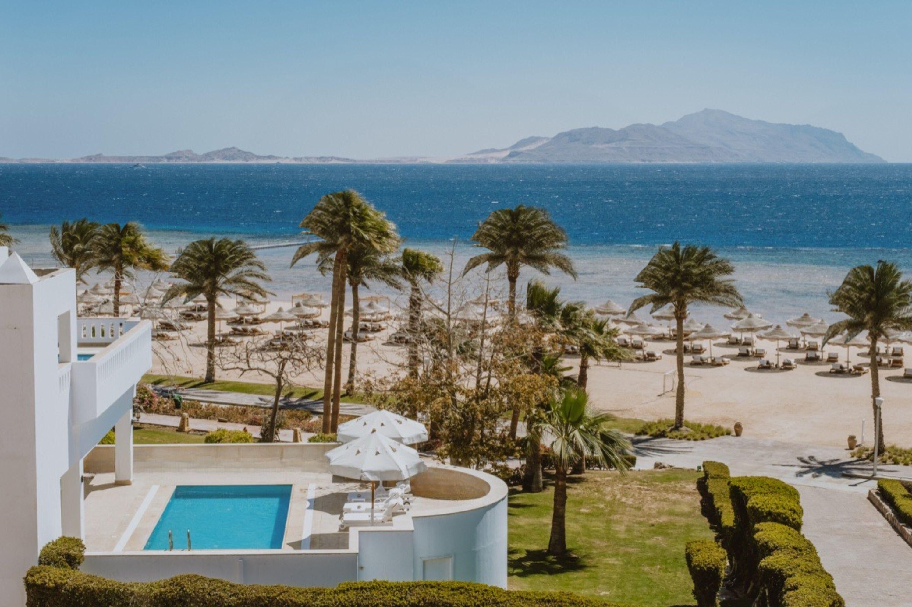 Um resort com piscina, palmeiras e vista para a praia.