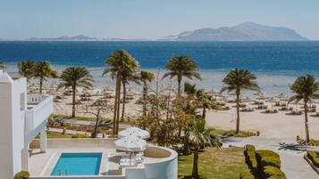 Um resort com piscina, palmeiras e vista para a praia.