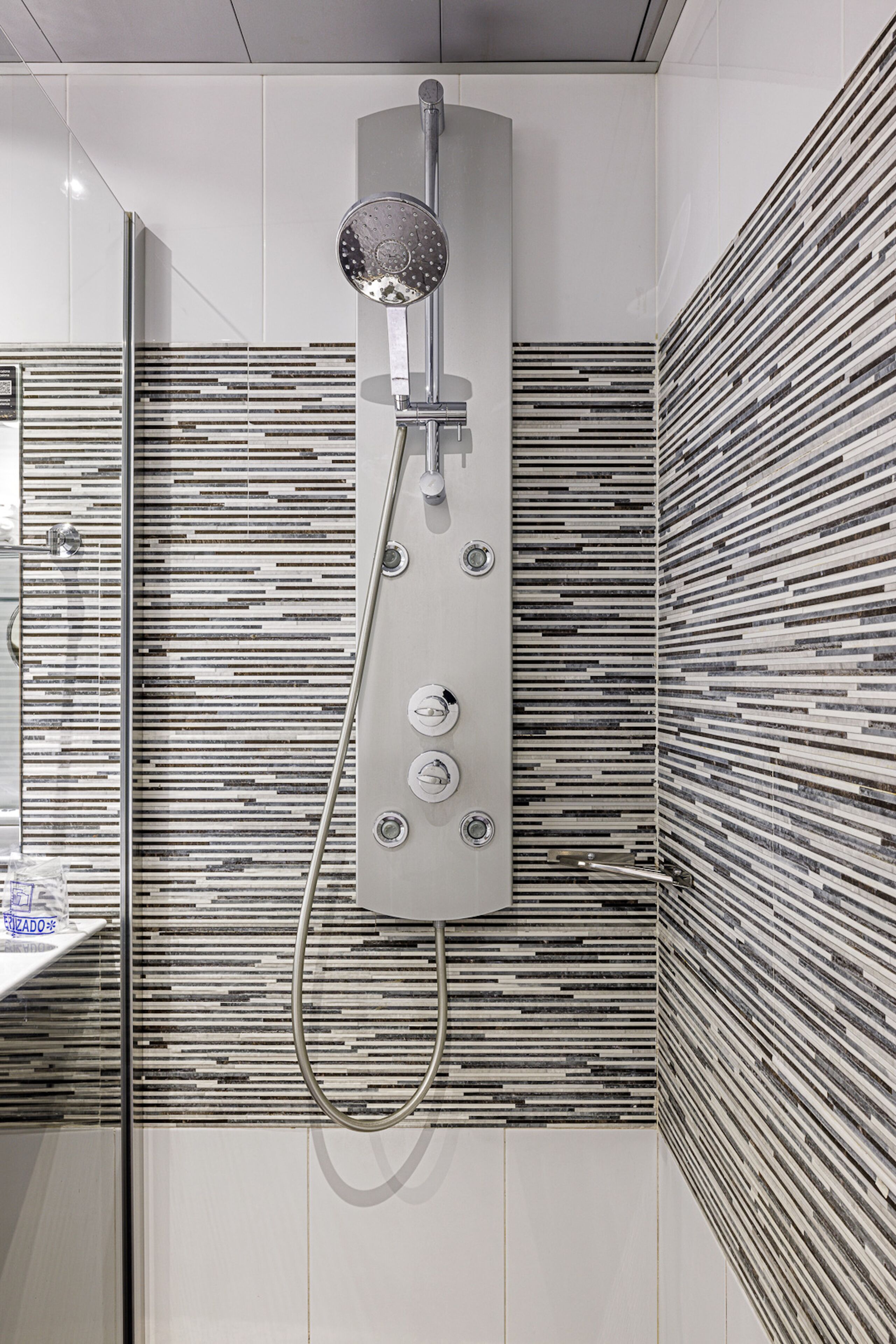 Chuveiro moderno com chuveiro de chuva e manípulos de controle, em frente a uma parede com padrão de azulejos listrados.