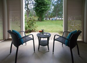 Estar coberto com móveis de vime e uma mesa, com vista para uma área gramada com árvores.
