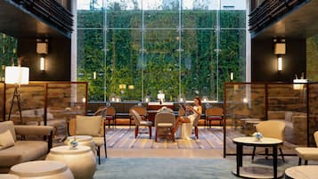 Uma área de estar moderna com uma janela grande que se abre para um jardim exuberante, mobiliada com sofás, poltronas e mesas.