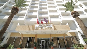Um hotel com fachada moderna, várias varandas e palmeiras.