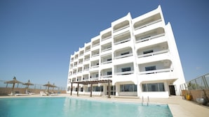 Hotel com vários andares e área de piscina, incluindo espreguiçadeiras e guarda-sóis.