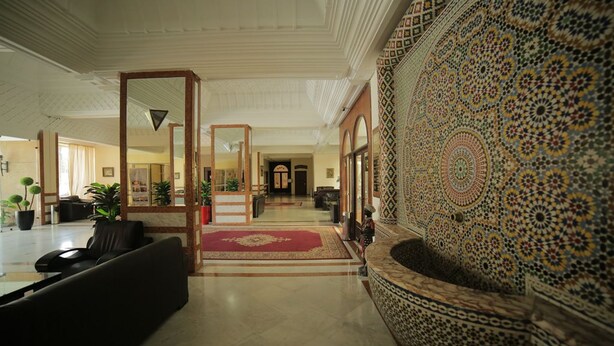 Um hall espaçoso com carpete vermelho, área de estar e uma parede decorativa com padrões elaborados.