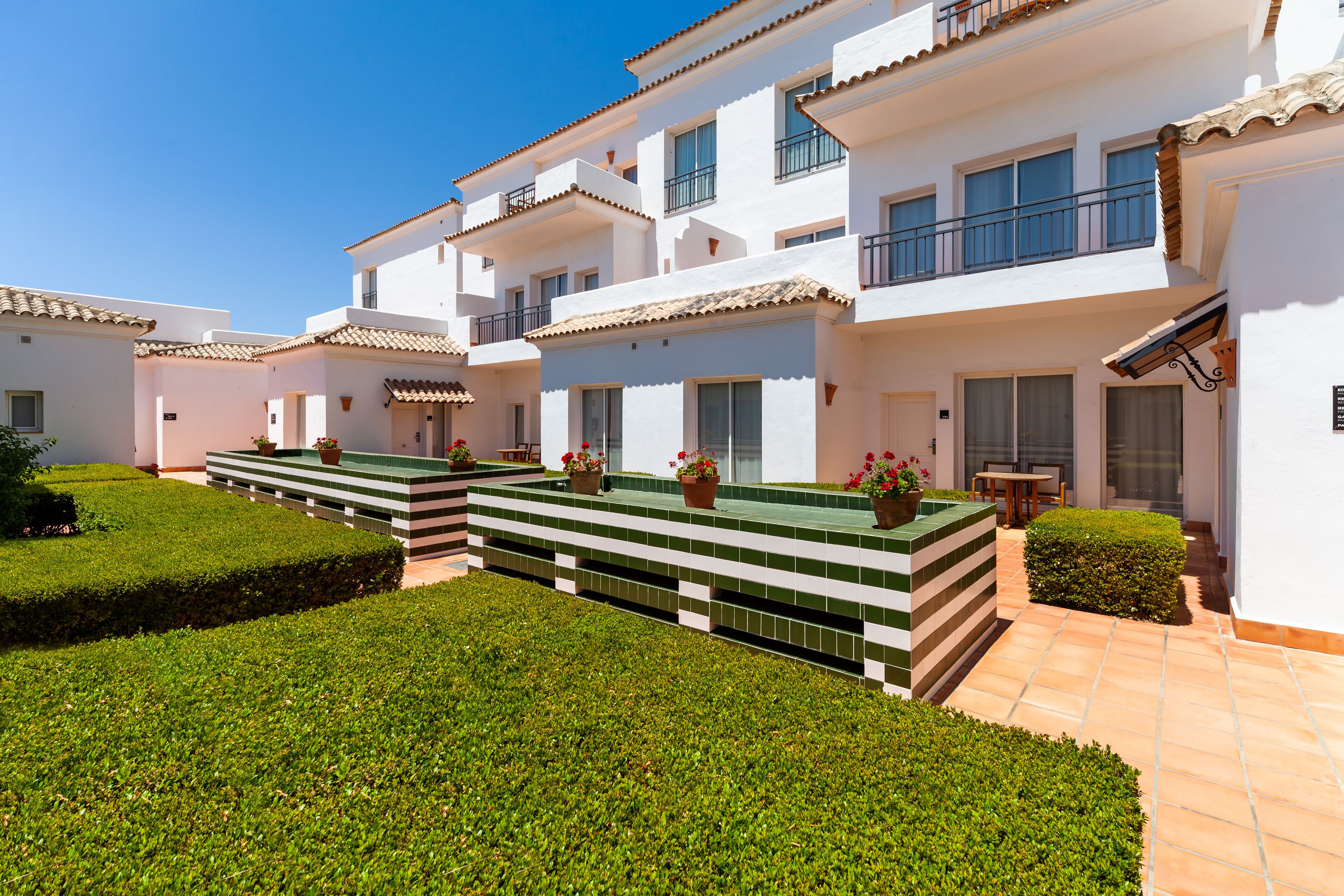Um edifício de vários andares com varandas, telhado telhado e um jardim bem cuidado.
