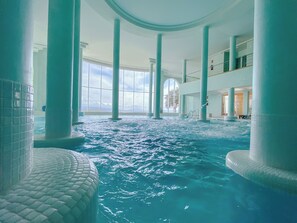 Piscina interior com água cristalina, rodeada por colunas imponentes e teto alto.