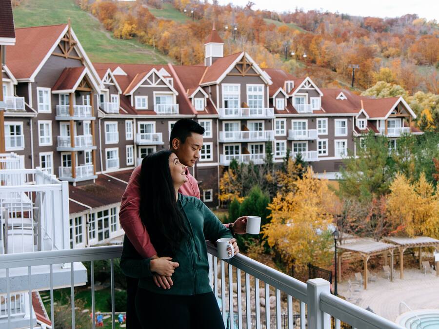 Um casal numa varanda com vista para um hotel com vários andares e zona de piscina.