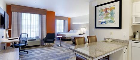 Quarto de hotel com cama, escrivaninha, cadeiras, mesa de jantar e cozinha.