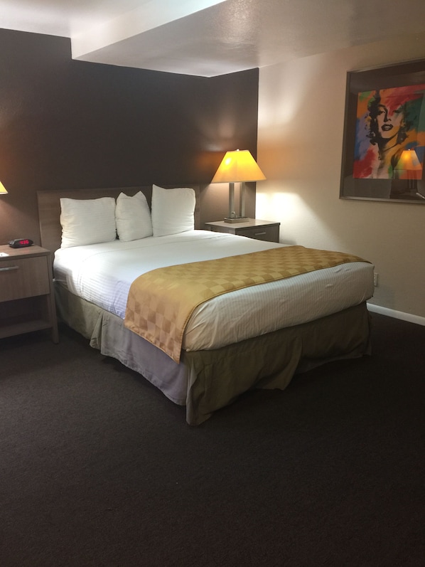 Quarto de hotel com cama, mesas de cabeceira, abajur e um quadro na parede.