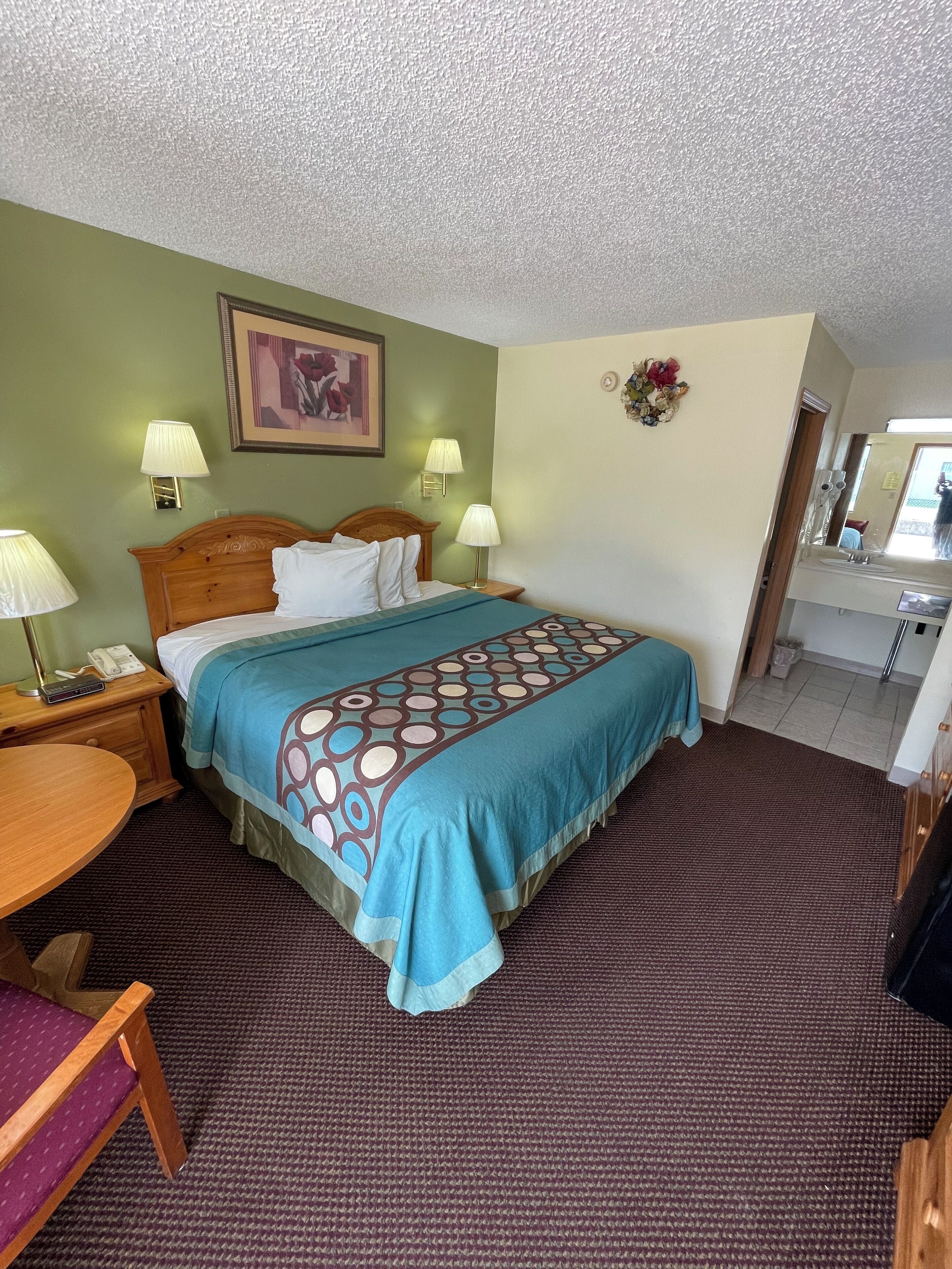 Quarto de hotel com uma cama, duas luminárias de cabeceira, um criado-mudo, uma escrivaninha e uma cadeira.