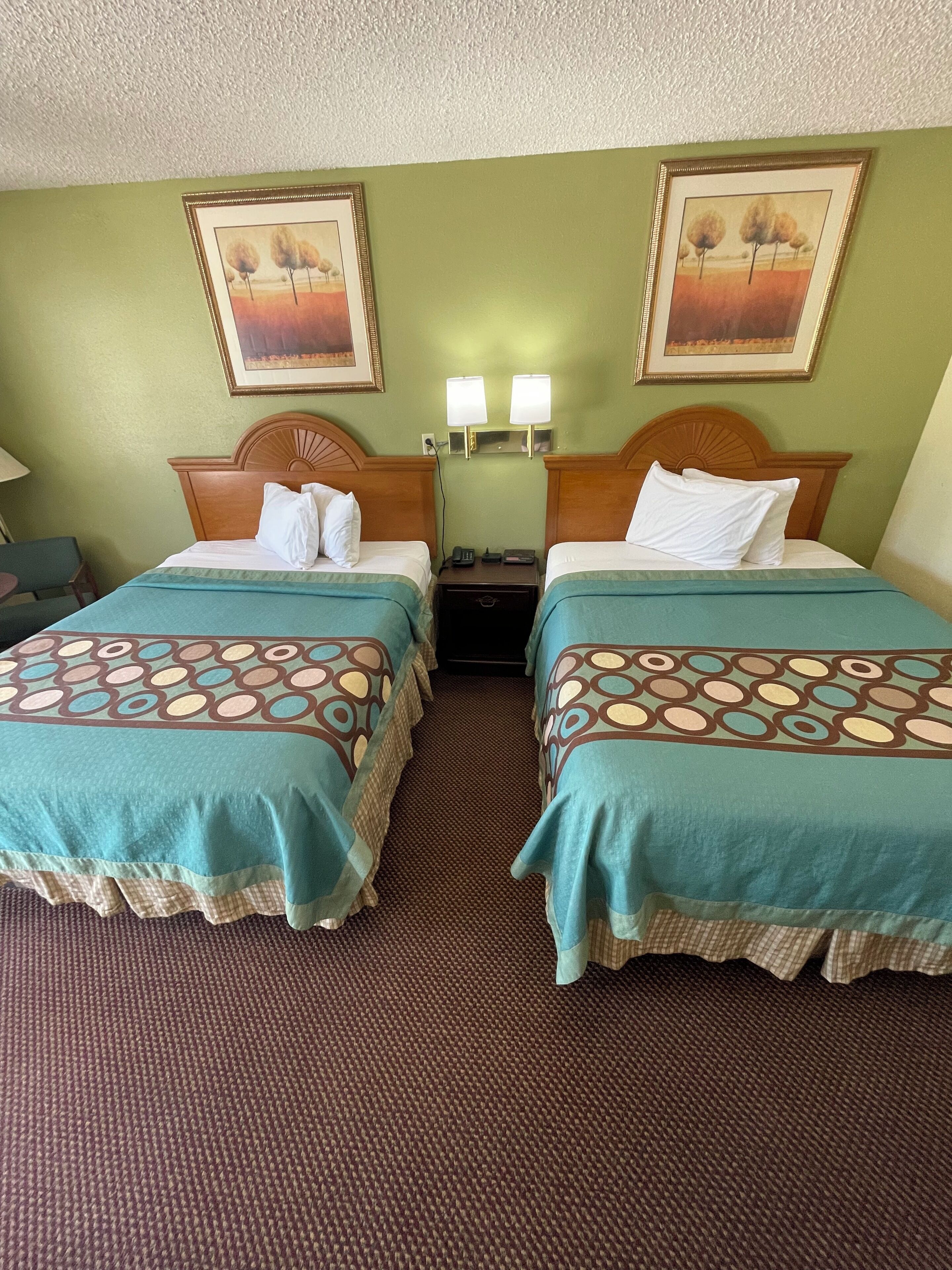 Quarto de hotel com duas camas, paredes verdes e duas pinturas emolduradas.