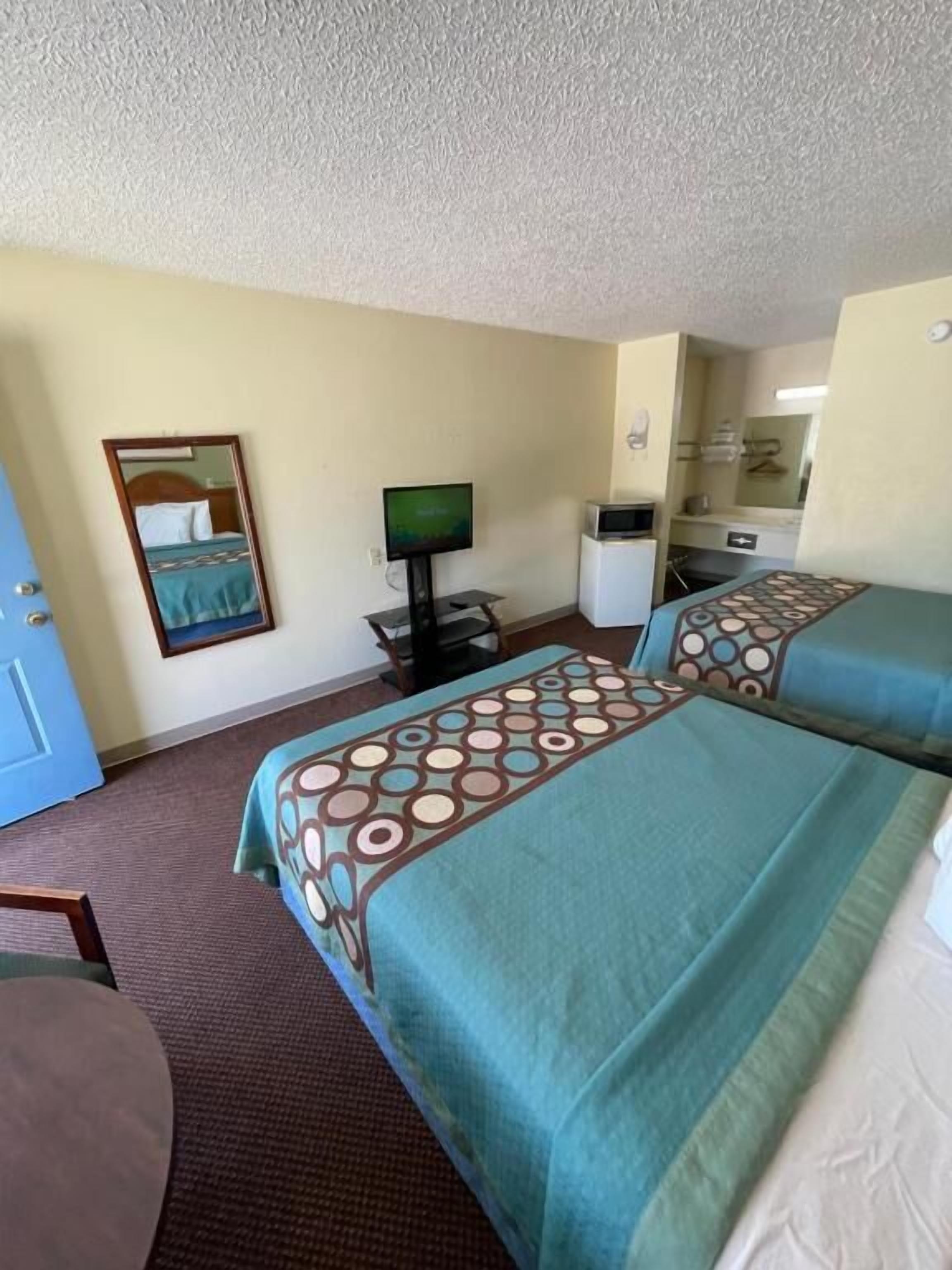 Quarto de hotel com duas camas, uma escrivaninha, televisão e cozinha compacta.