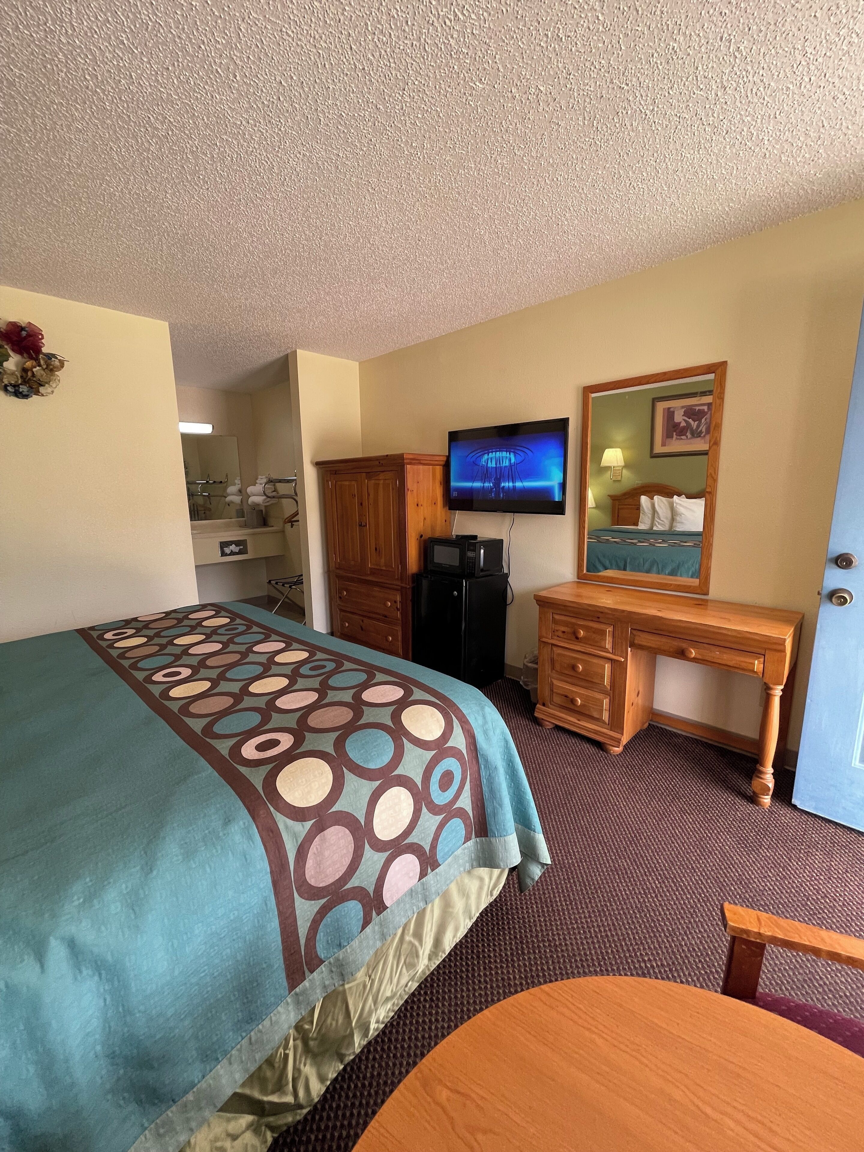 Quarto de hotel com cama, escrivaninha, televisão e espelho.