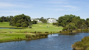Um campo de golfe com lago, árvores e edifícios ao fundo.