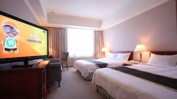 Quarto de hotel com duas camas, televisão, escrivaninha e uma cadeira.