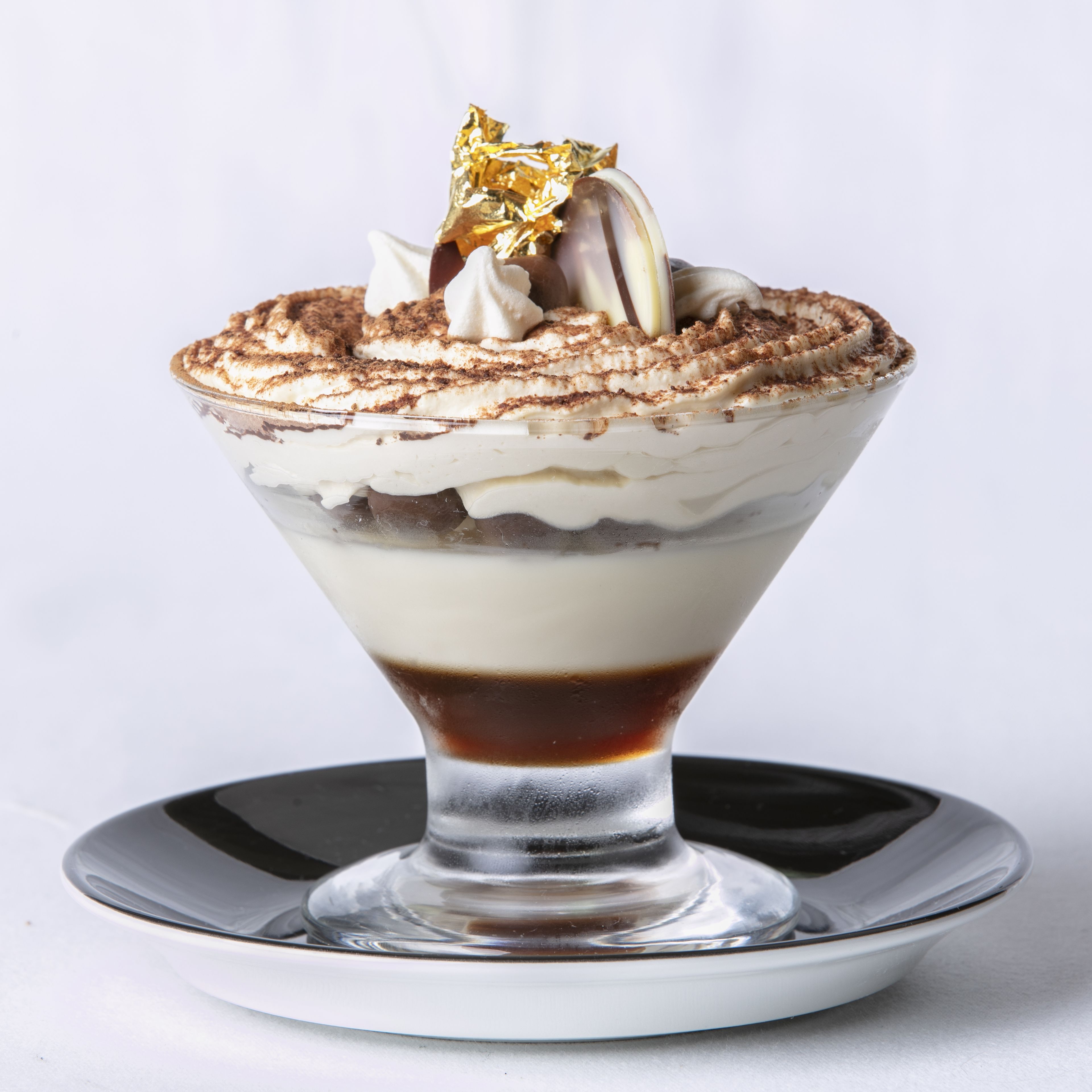 Sobremesa em taça de vidro com camada de chocolate, chantilly e folha dourada como guarnição.