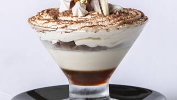 Sobremesa em taça de vidro com camada de chocolate, chantilly e folha dourada como guarnição.
