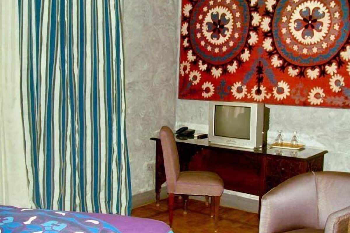 Quarto de hotel com cama, escrivaninha com computador, cadeira e televisão.