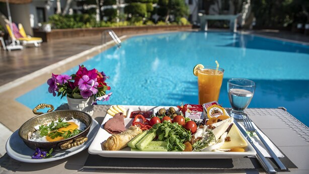 Uma mesa de jantar com um prato de comida, um copo de suco de laranja e um copo de água, tudo junto a uma piscina.