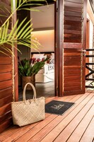 Uma porta de madeira com um tapete, uma bolsa tecida e um vaso de planta em um deck de madeira.