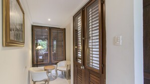 Um corredor com uma porta de madeira, um quadro na parede e duas cadeiras perto de uma janela.