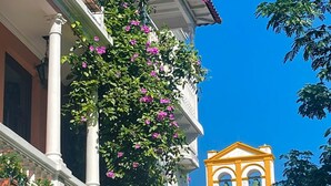 Um edifício com varanda decorada com plantas floridas e uma torre de sino com estátua.