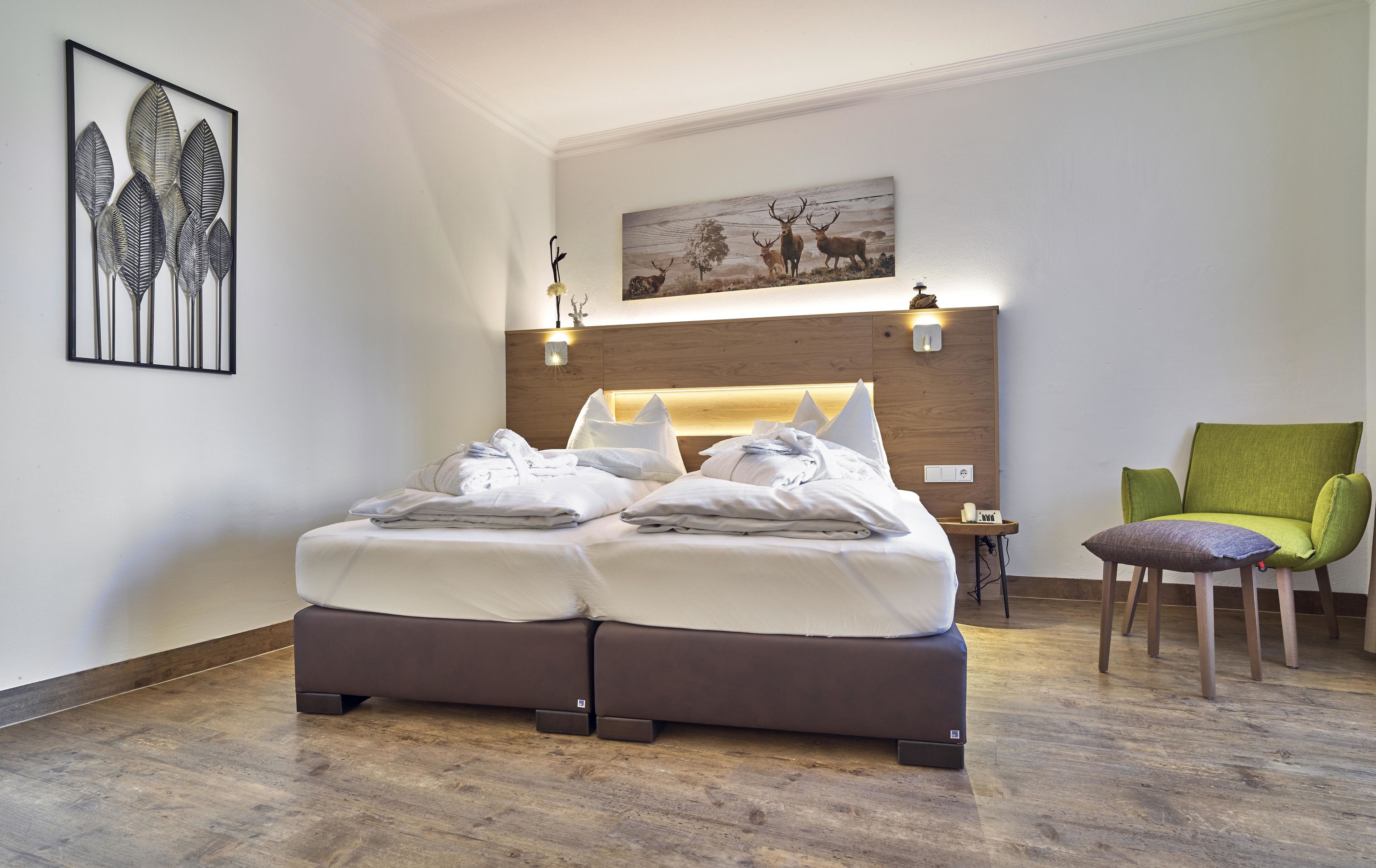 Quarto de hotel moderno com uma cama grande, uma poltrona verde e um quadro pendurado na parede.