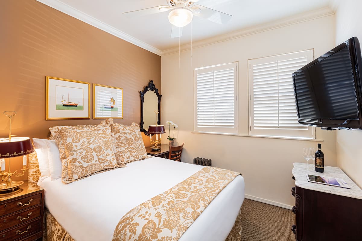 Quarto de hotel com uma cama grande, televisão de tela plana, escrivaninha com luminária e duas fotos emolduradas na parede.