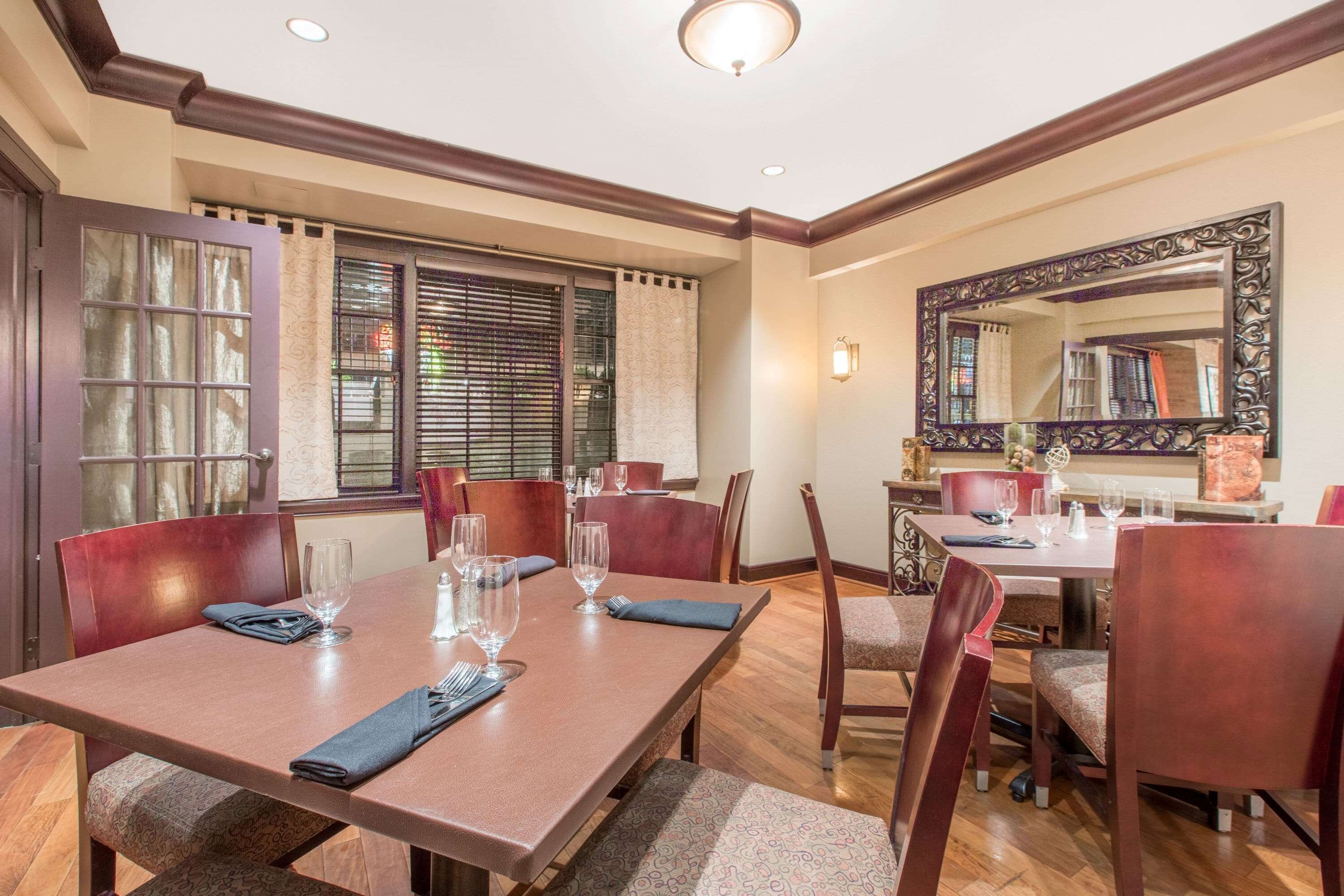 Uma sala de jantar com uma mesa posta para quatro pessoas, cadeiras de madeira e um espelho grande acima da mesa.