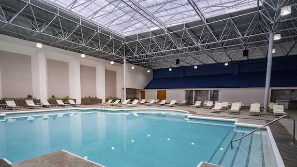 Piscina interna com teto de vidro, cercada por espreguiçadeiras e piso revestido de azulejos.
