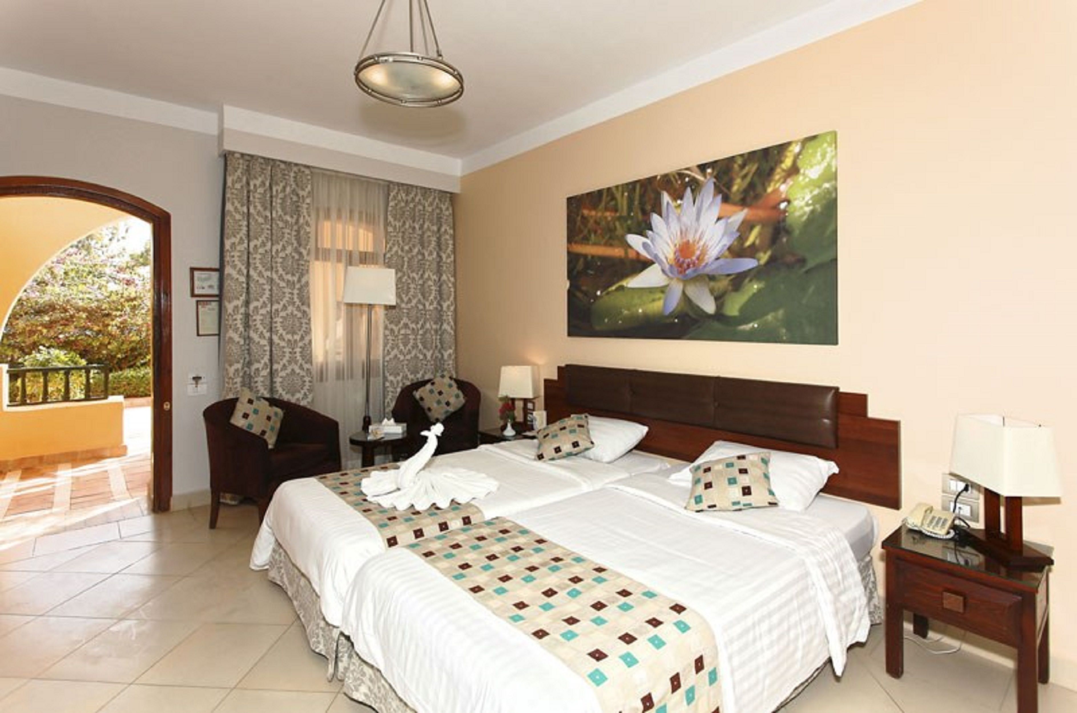 Quarto de hotel com uma cama grande, duas mesas de cabeceira, uma cadeira, uma escrivaninha e uma janela com cortinas.